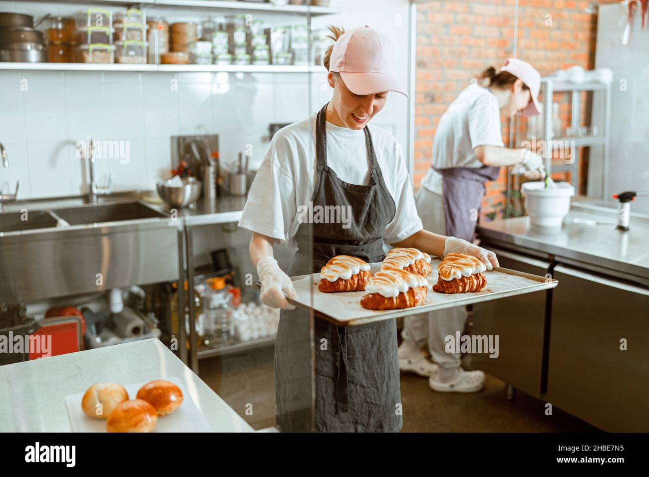 Smiling woman holds tray with delicious croissants decorated with burnt ...