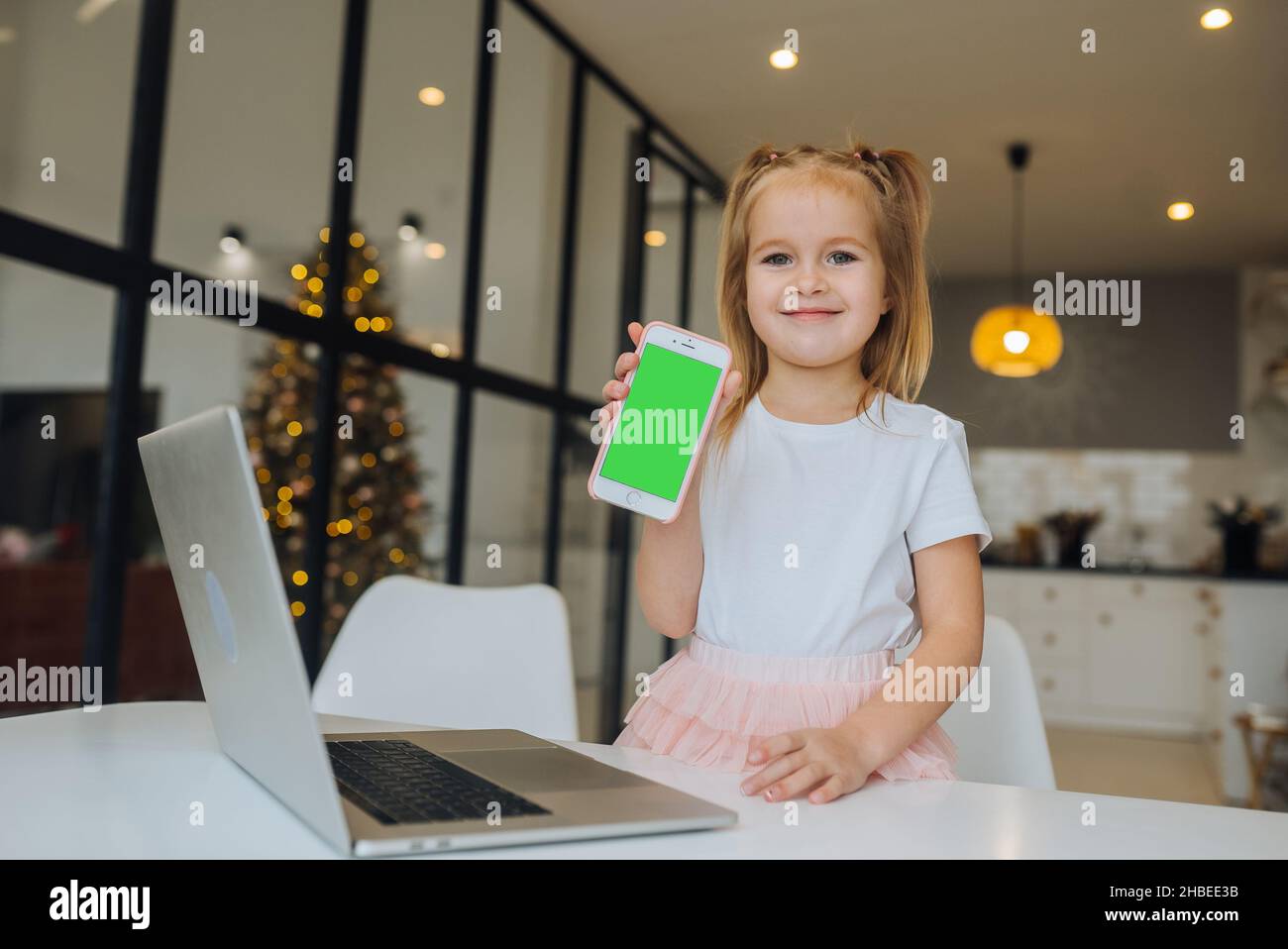 Little kid sit at desk with laptop hold mobile phone Stock Photo - Alamy