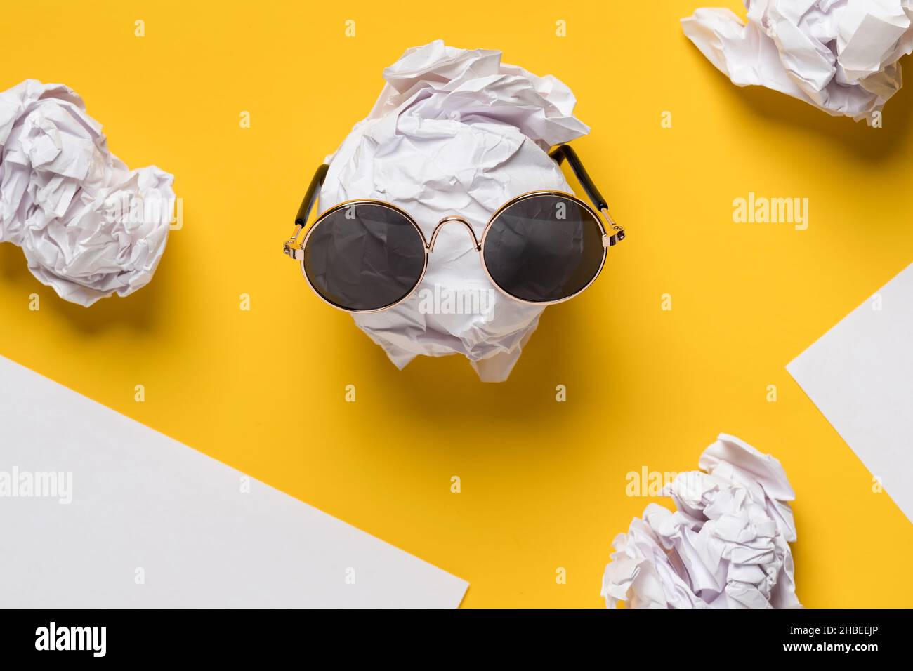 Crumpled paper and sunglasses on it look like a face, next to white ...