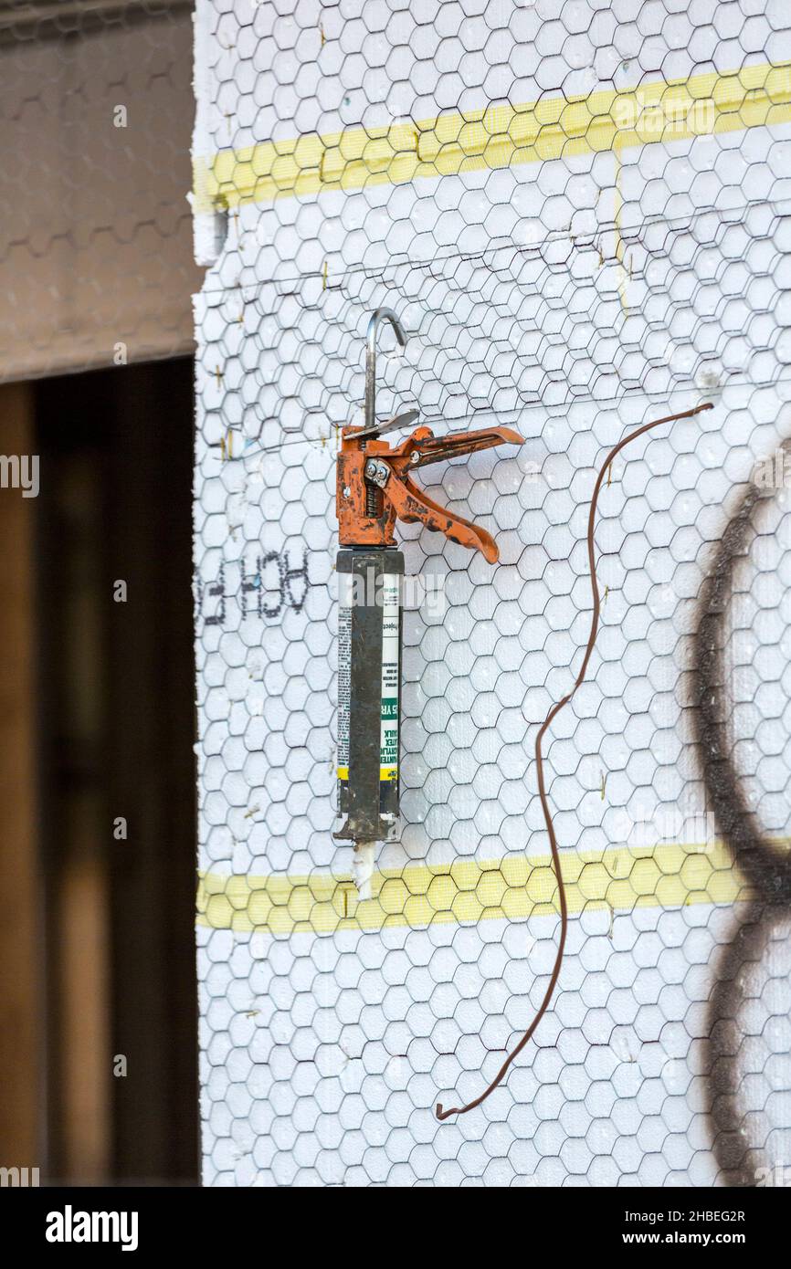 Caulk gun hanging on a wall covered in metal construction mesh Stock ...