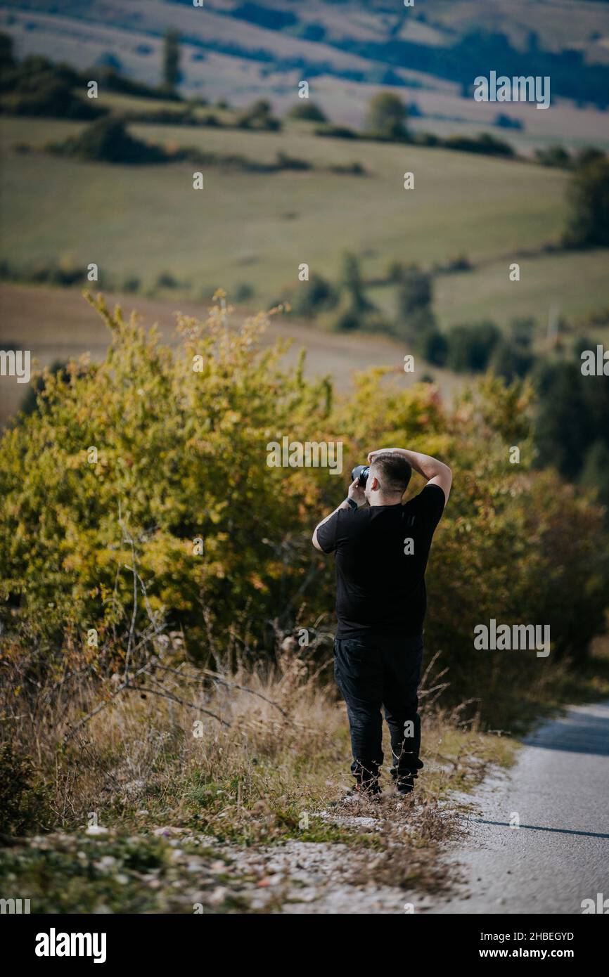 A vertical shot of a young photographer with his camera in nature ...