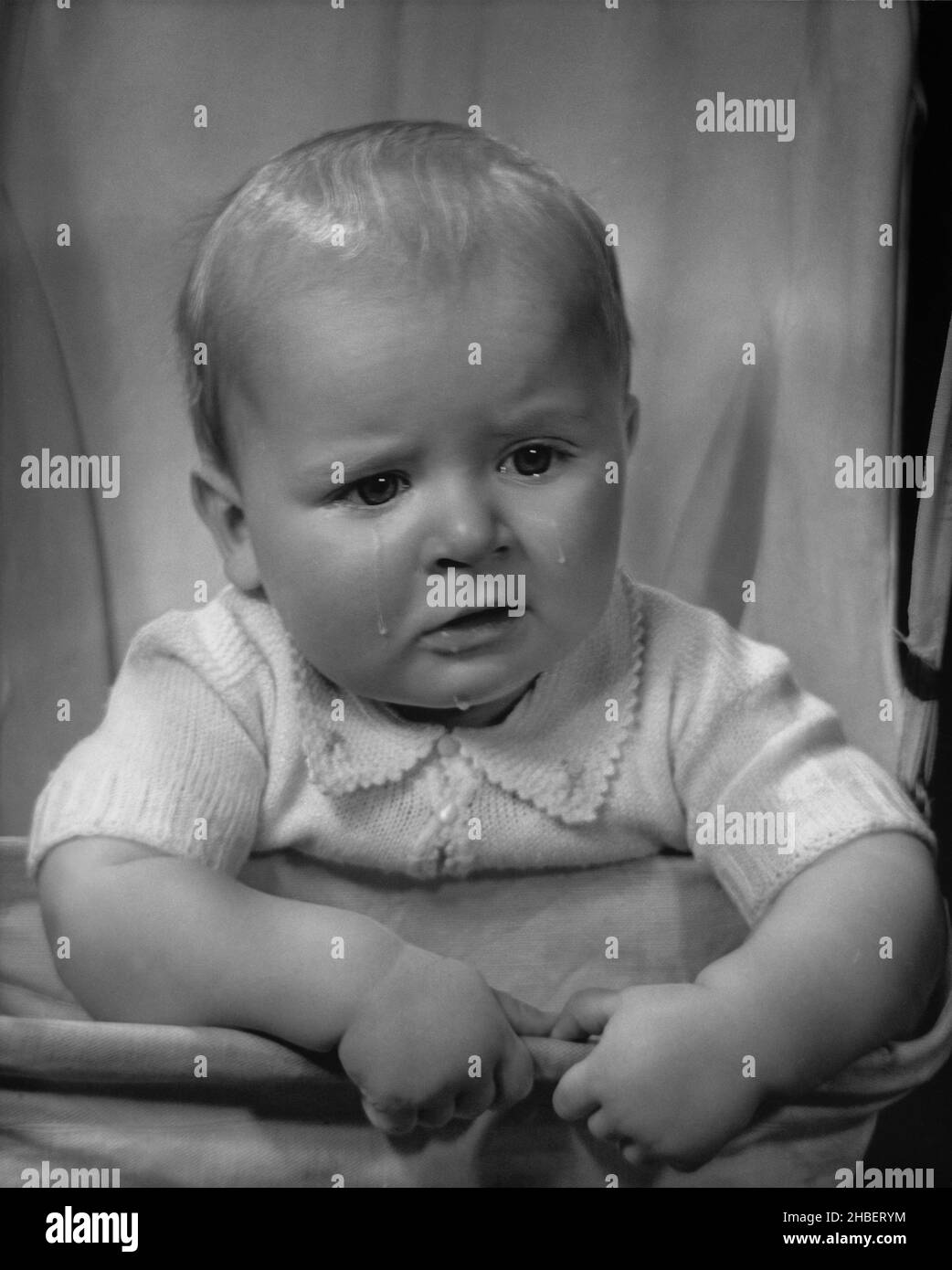 Infant sitting in a swing glancing down with tears running down his ...