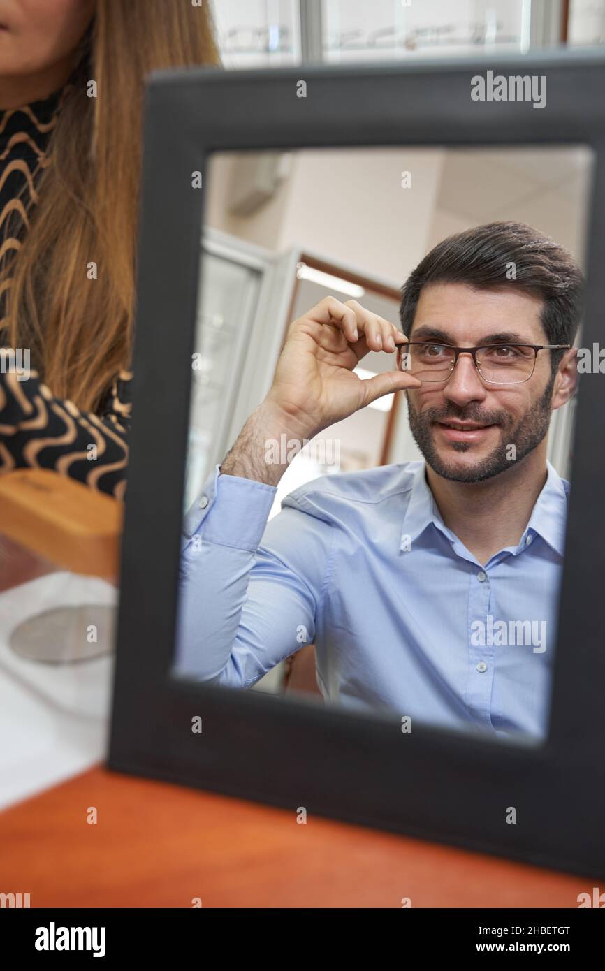 Man checking his appearance with glasses in a mirror Stock Photo - Alamy