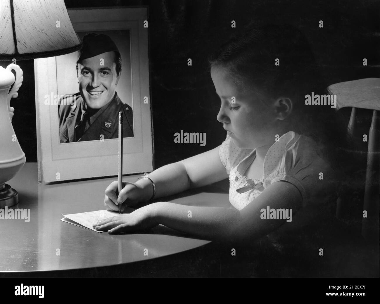 Little girl writing a letter to her dad in the military while picture ...