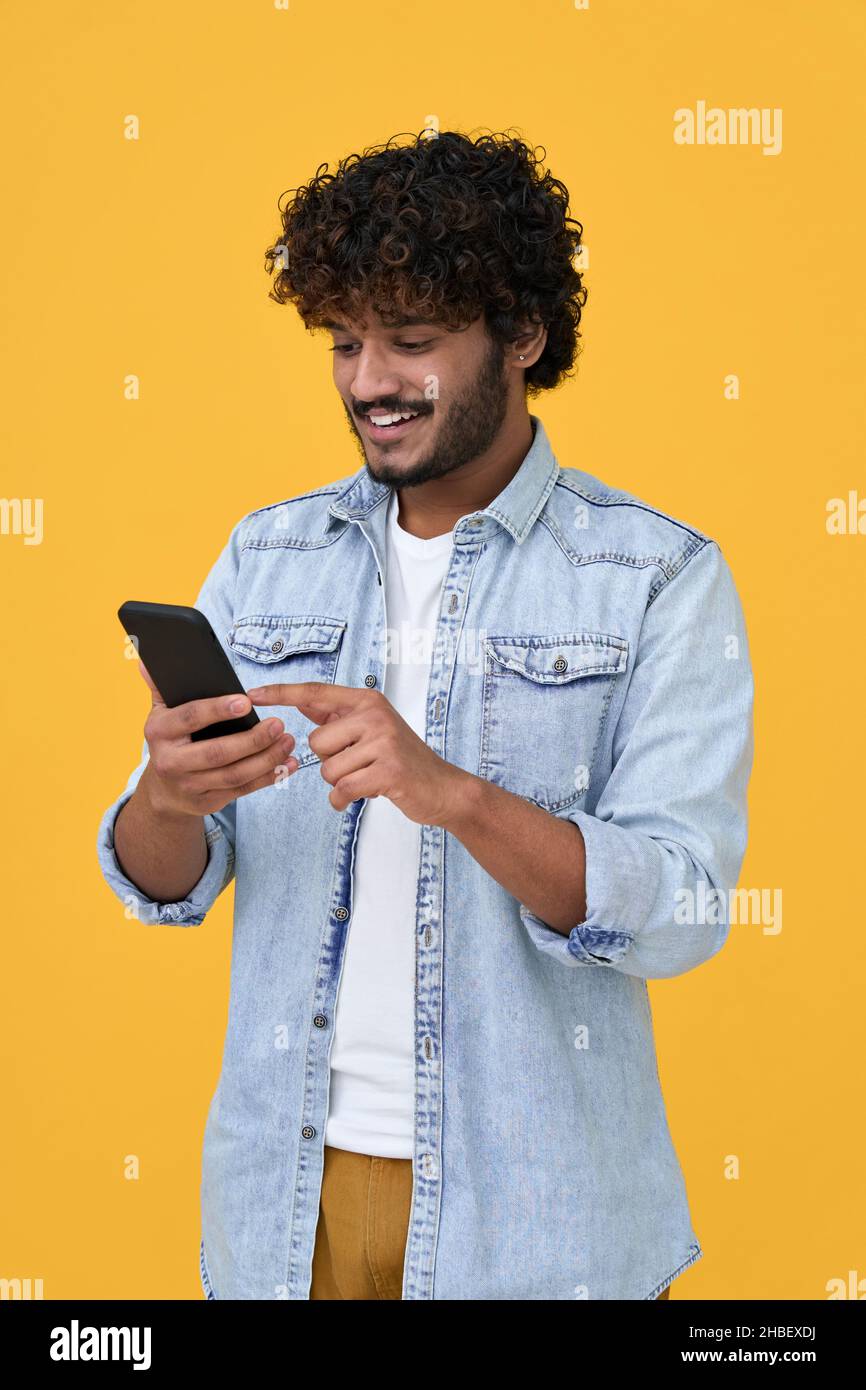 Happy indian young man using cell phone isolated on yellow background ...