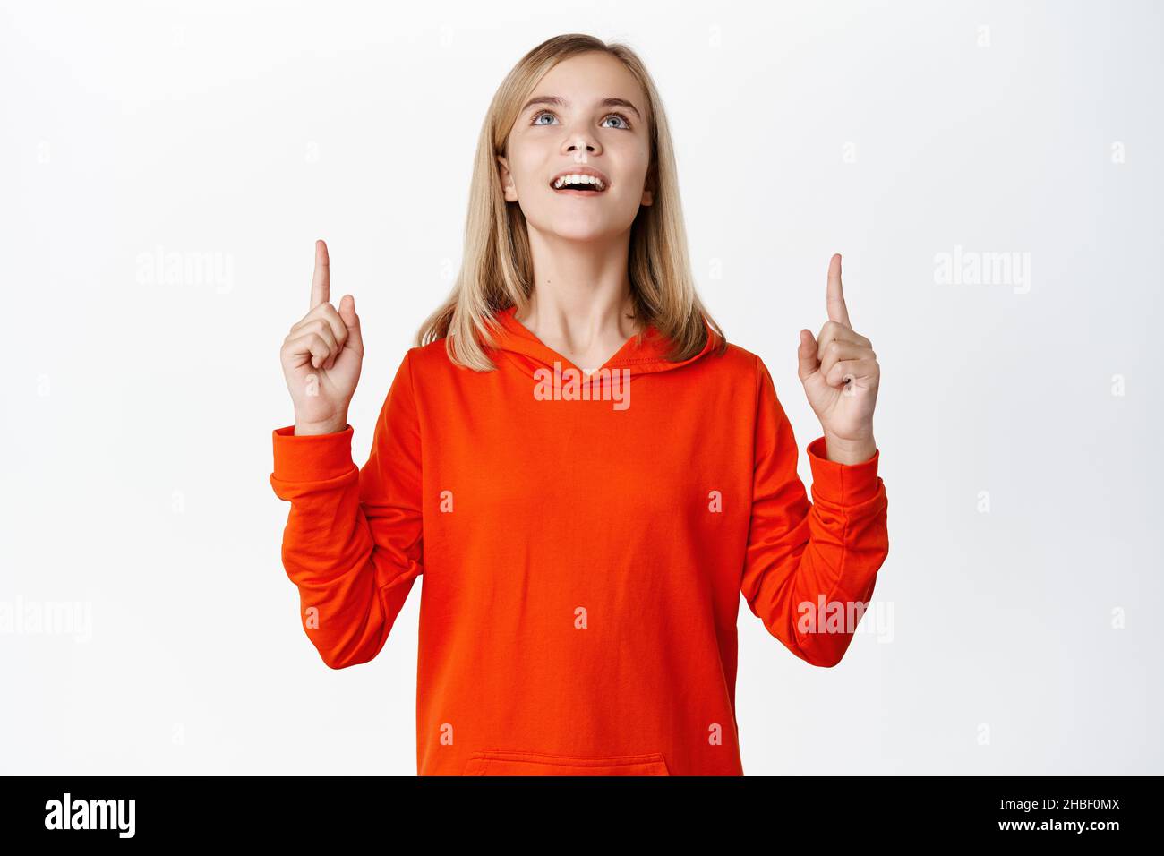 Amazed little girl pointing fingers up and smiling, staring at sky with ...