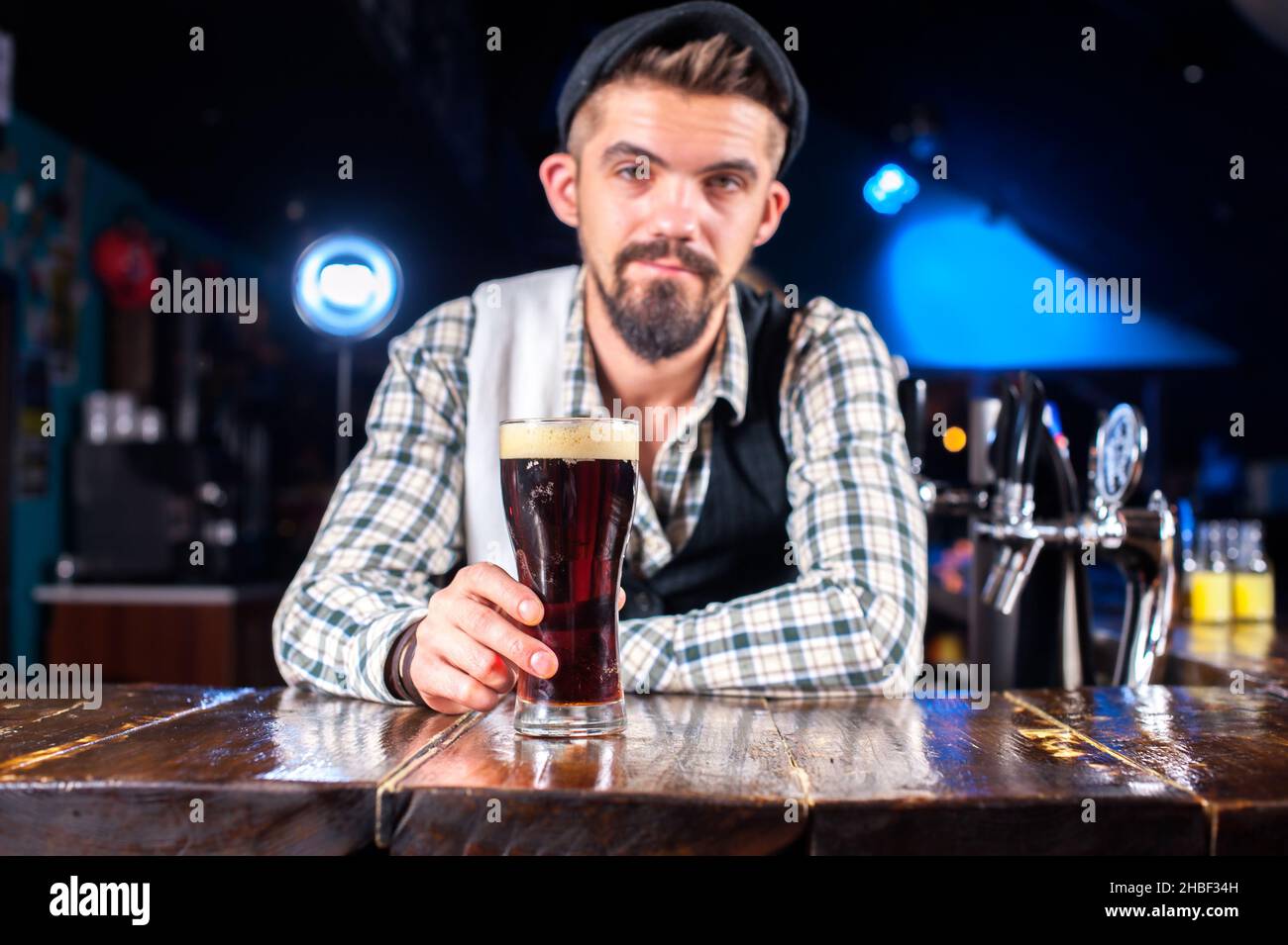 Young bartending pouring fresh alcoholic drink into the glasses while standing near the bar ...