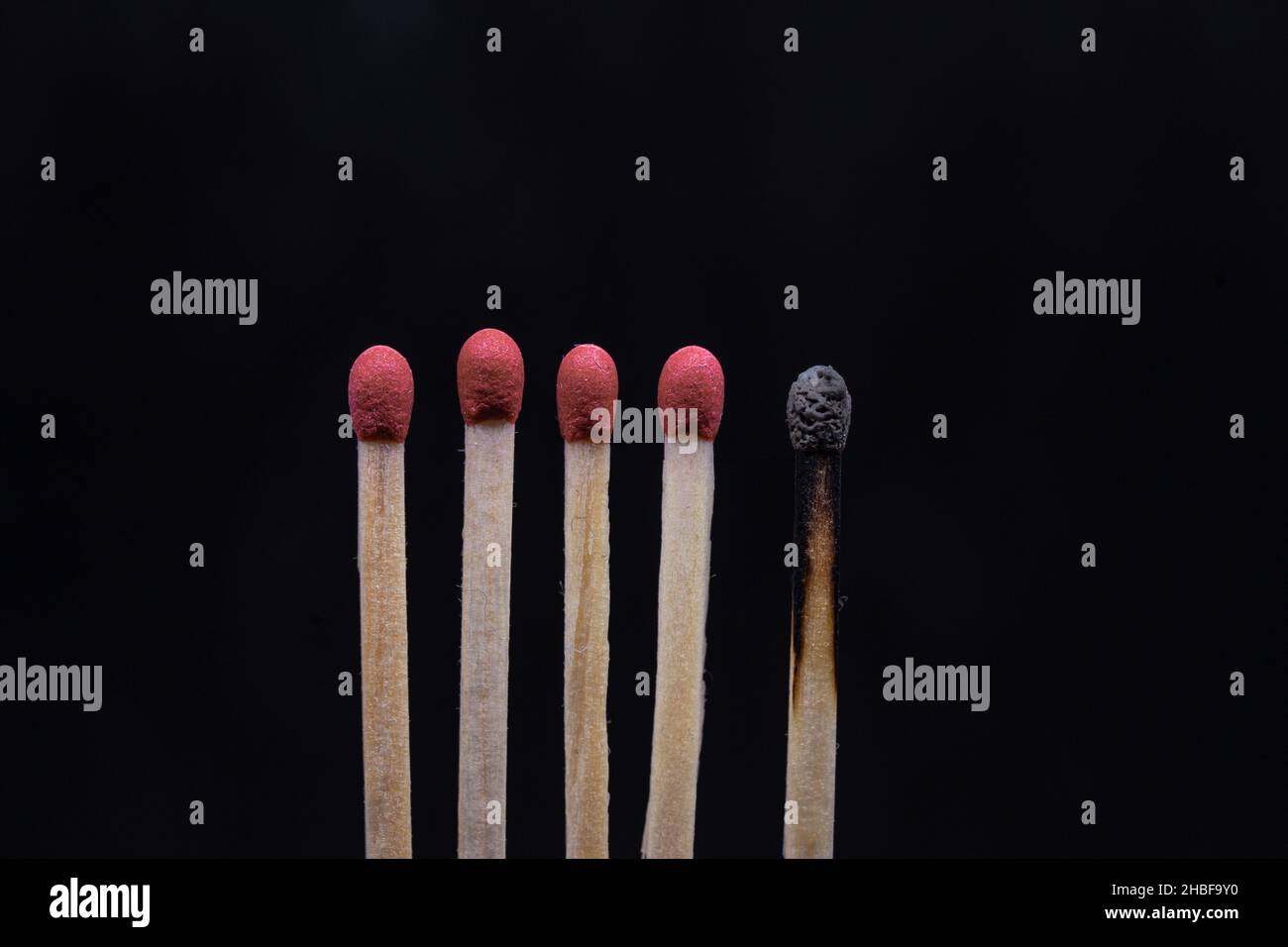 A closeup of four matches and a used one aligned with isolated black ...