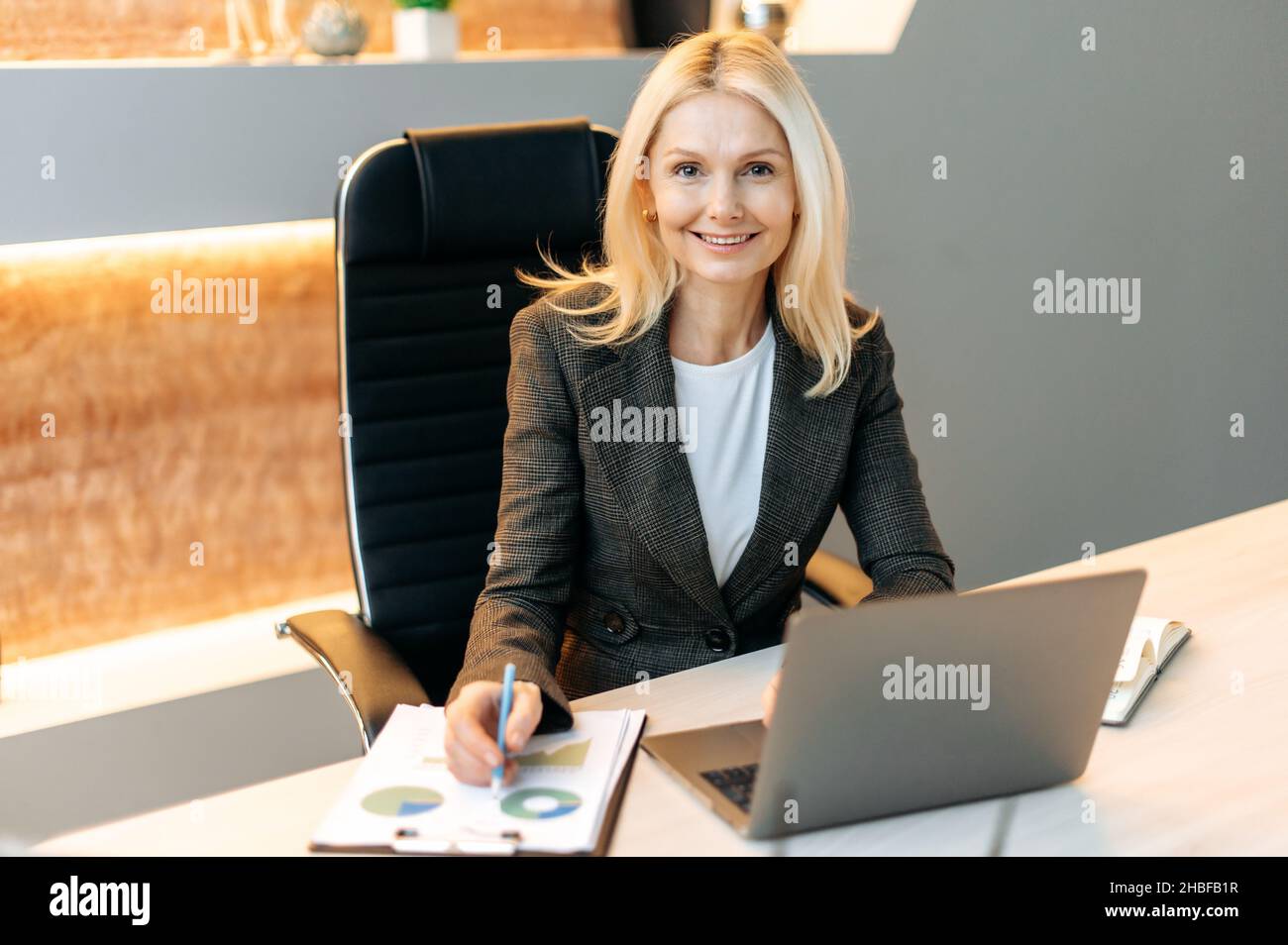 Portrait of pretty mature female employee is sitting at the desk in ...
