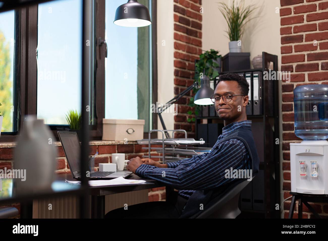 Startup worker posing confident sitting at desk with laptop and looking ...