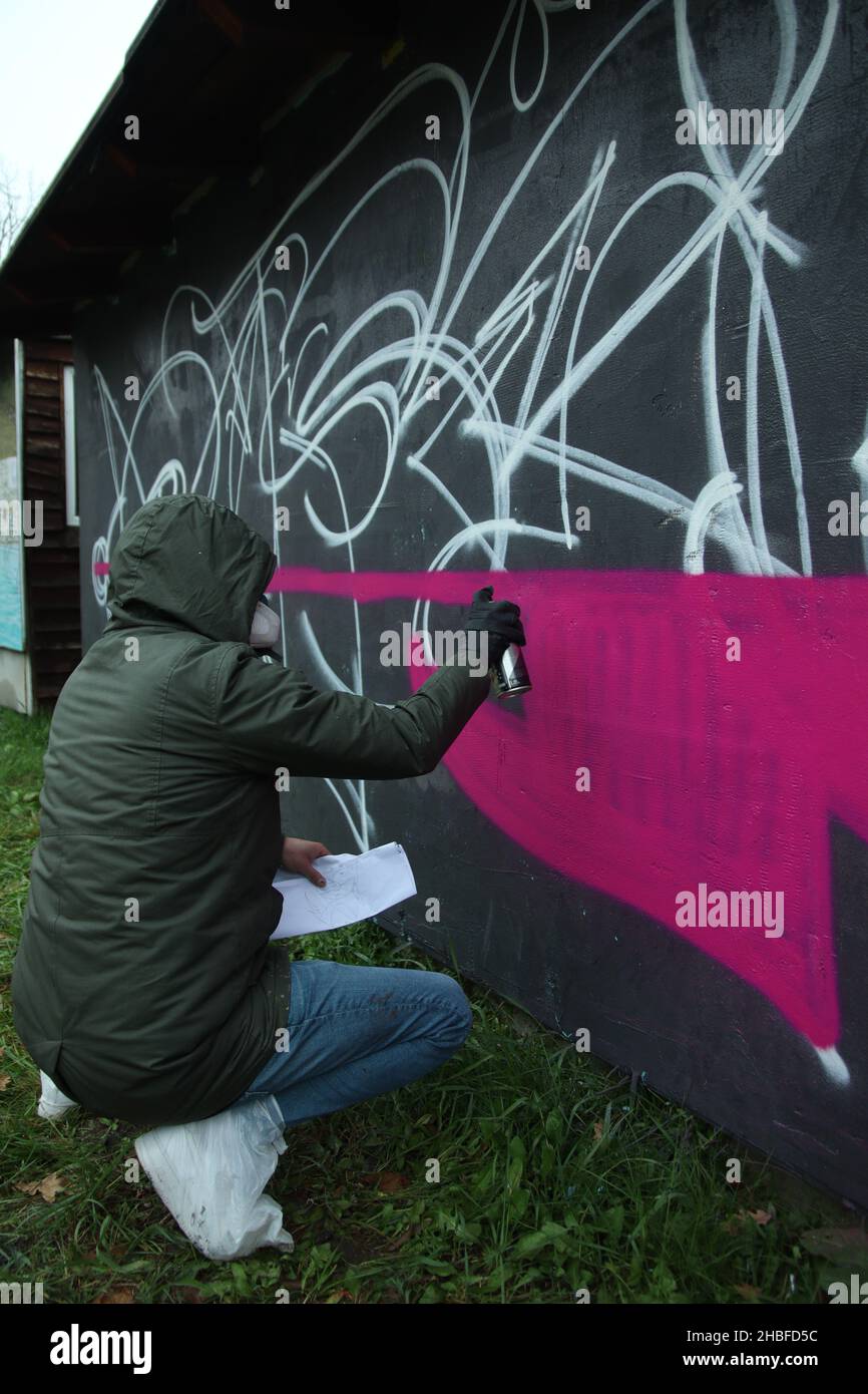 A vertical shot of a male doing a graffiti on wall kneeling on the ...