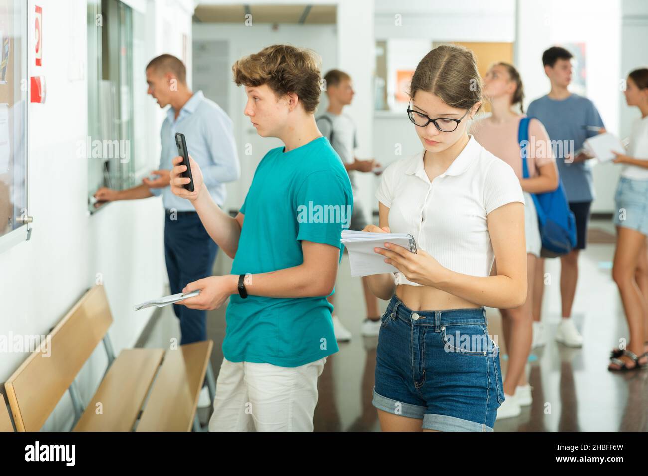 Teenage students checking exam schedule on bulletin board in college ...
