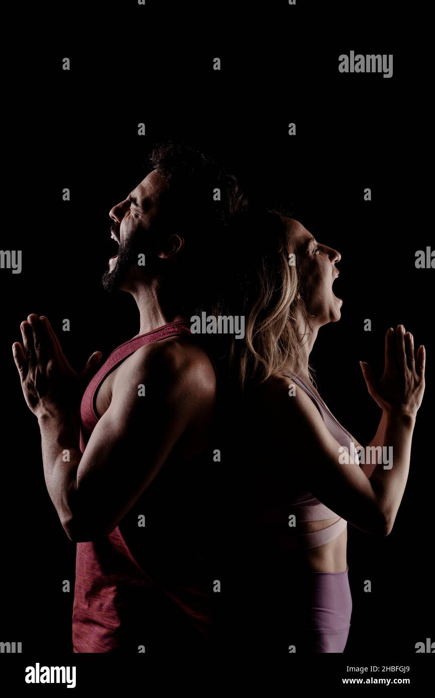 Fit couple posing together. Boy and girl praying back to back side lit ...