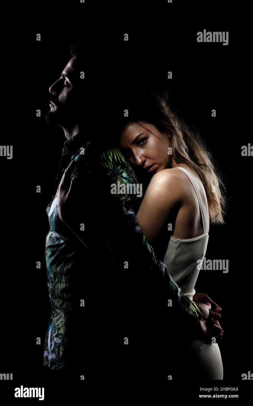 Couple posing on black background. Girl hugging boy in shadow from ...