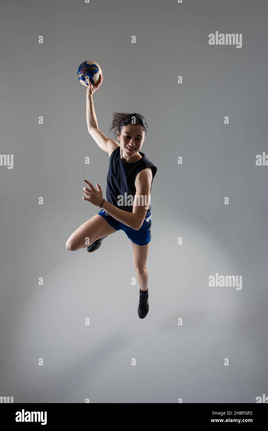 Handball player posing on light gray background. Girl jumping with ball ...