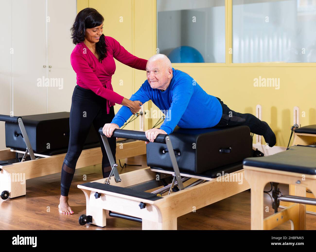 Senior man doing pilates on reformer with Hispanic female trainer Stock ...