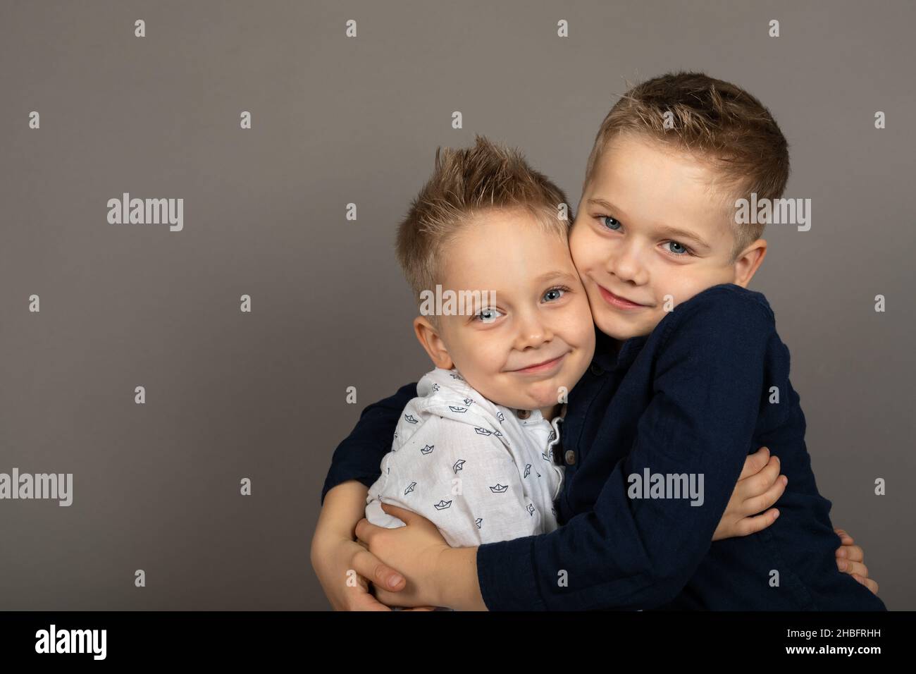 Two brothers hugging each other in front of a grey background Stock ...