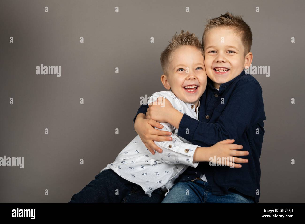 Two brothers hugging each other in front of a grey background Stock ...