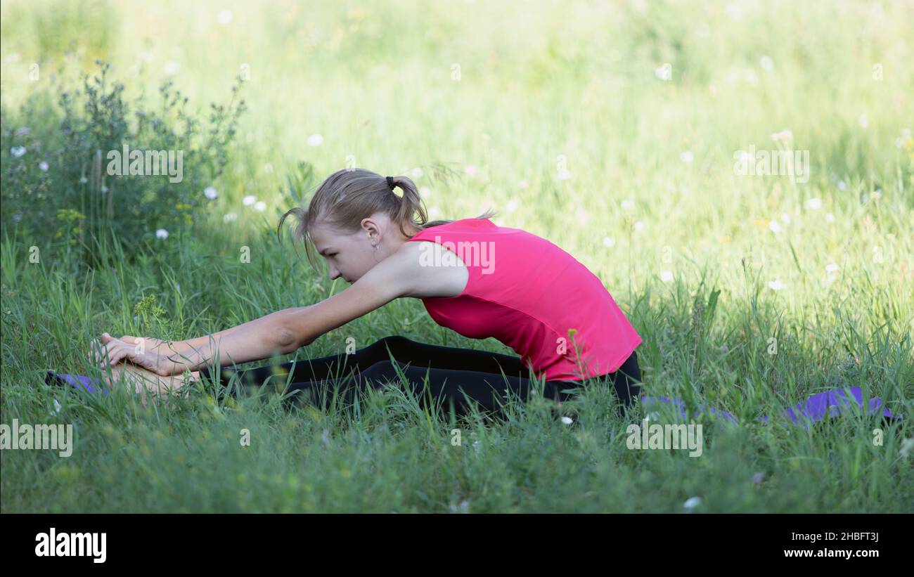 Side view of young blonde caucasian girl stretching on green grass of ...