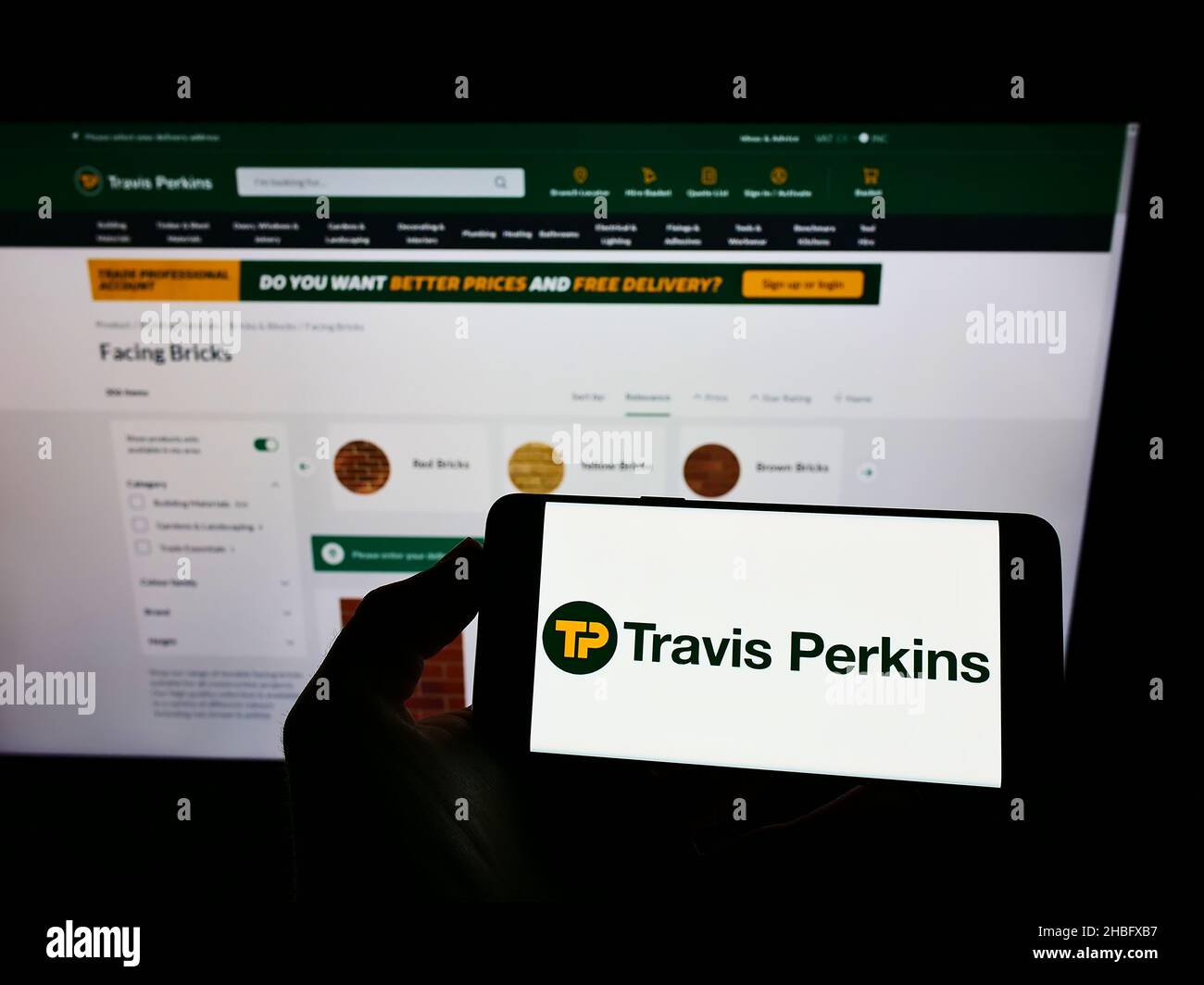 Person holding cellphone with logo of British retail company Travis Perkins plc on screen in ...