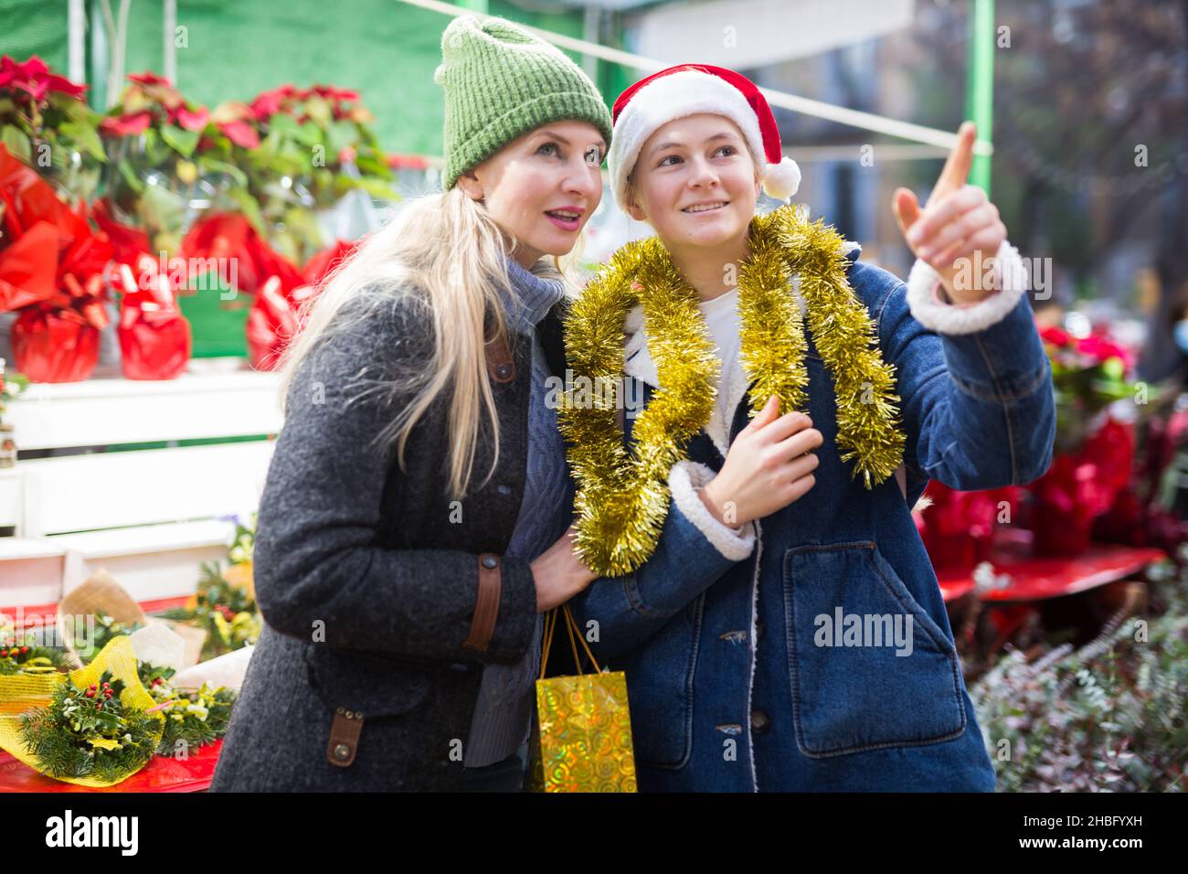 Daughter points her hand to mom as they walk through street Christmas ...