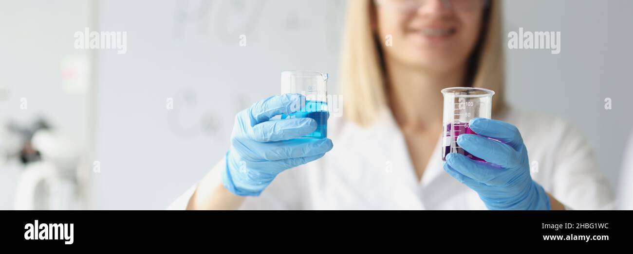 Woman chemist holding glass beakers with pink and blue liquid in front ...
