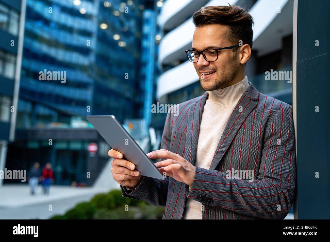Happy young business man with tablet at work in modern urban background ...