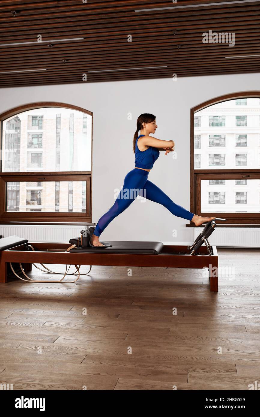 Young girl doing pilates exercises with a reformer bed. Beautiful slim ...