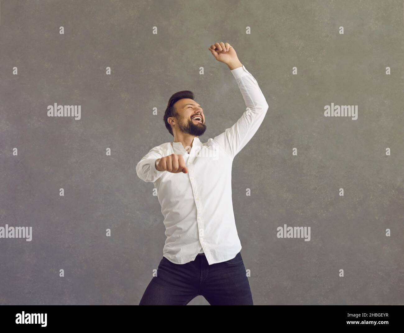 A happy cheerful young man dancing gangnam style against a grey studio ...