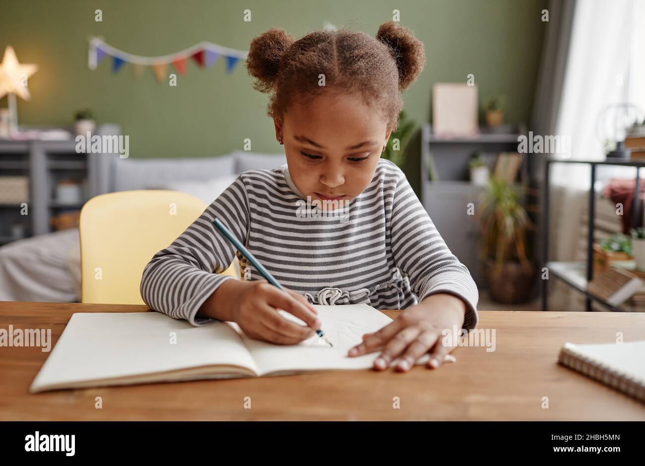 Front view portrait of cute African-American girl doing homework while ...