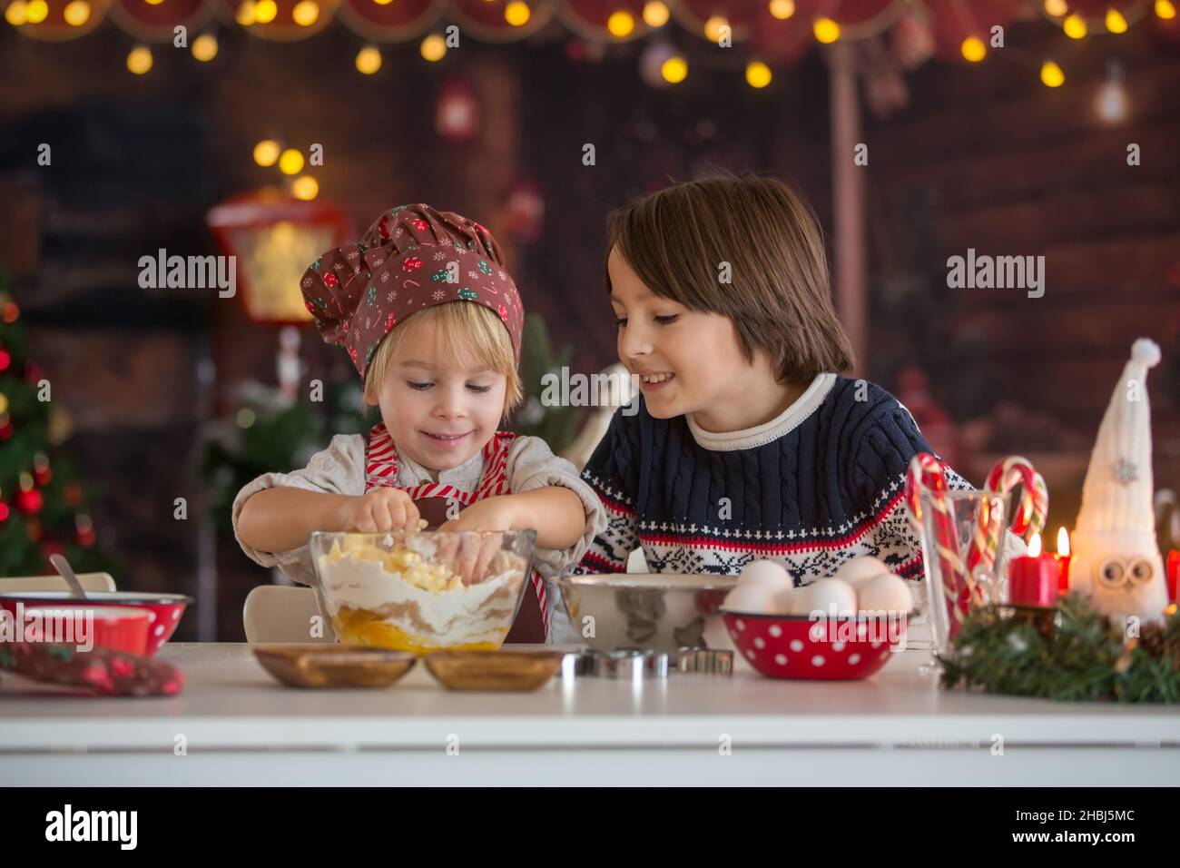 Cute blond child and his brothers, baking christmas cookies at home ...