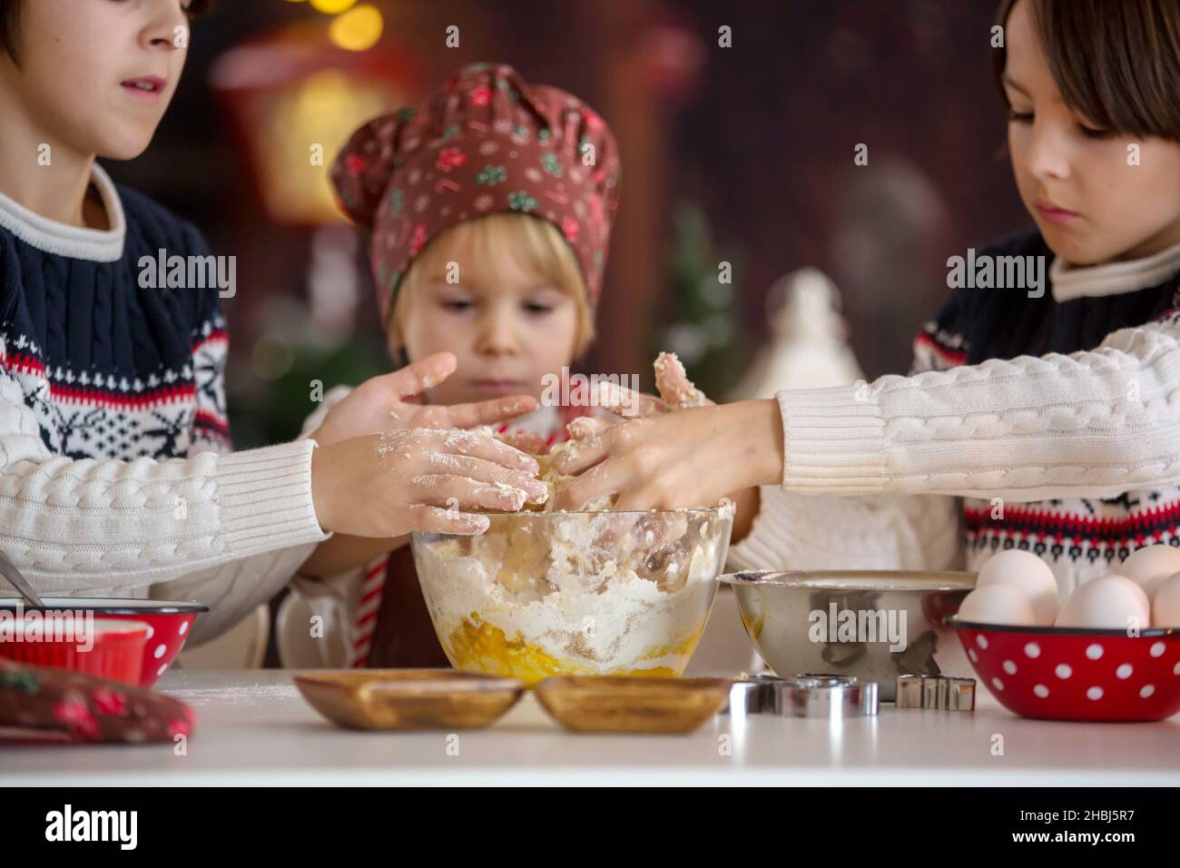 Cute blond child and his brothers, baking christmas cookies at home ...