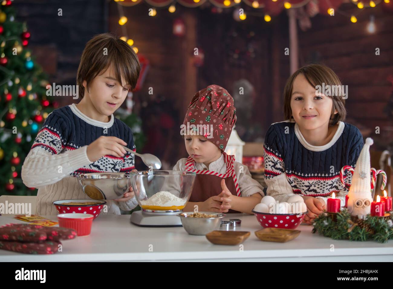 Cute blond child and his brothers, baking christmas cookies at home ...