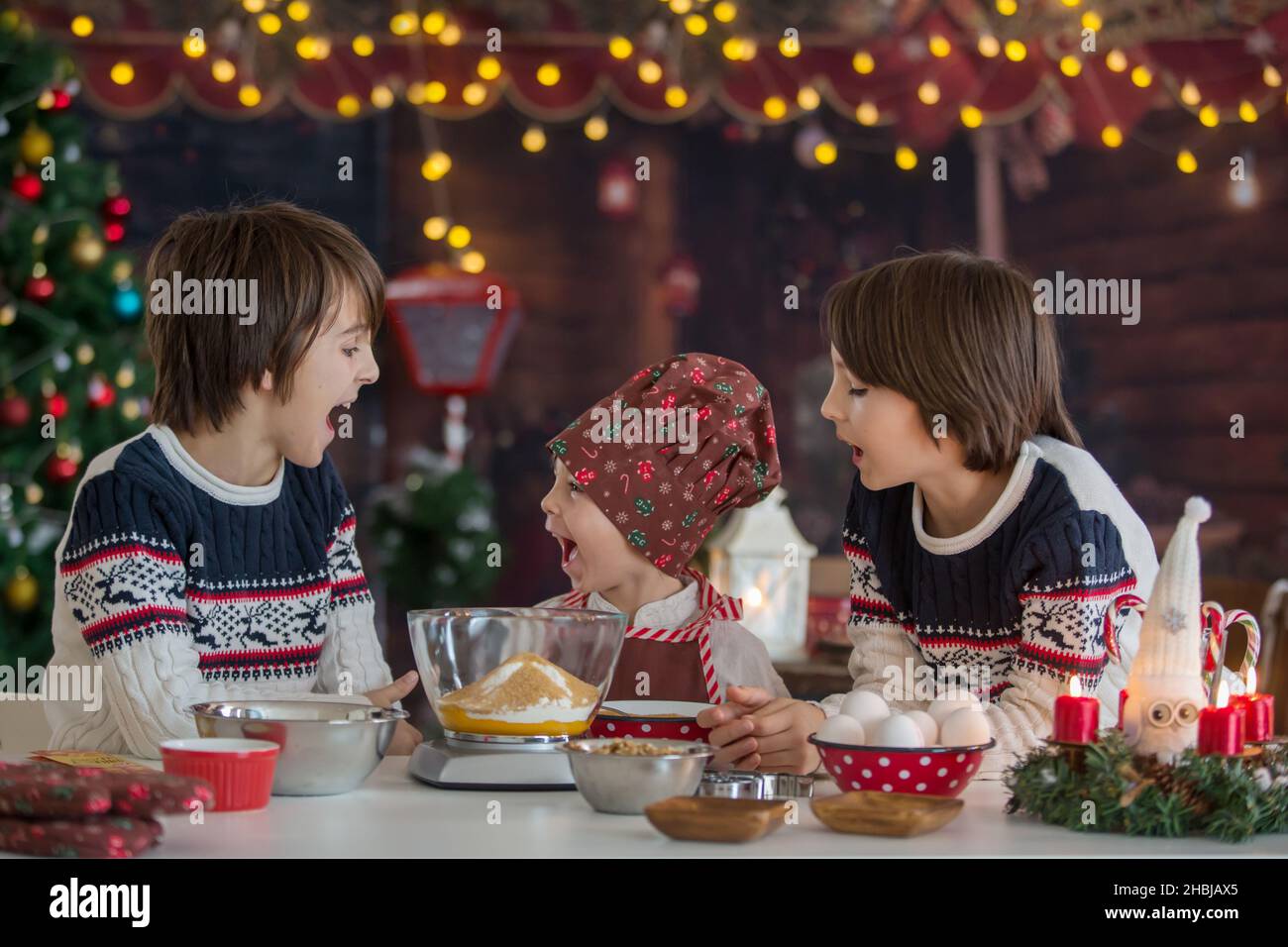 Cute blond child and his brothers, baking christmas cookies at home ...