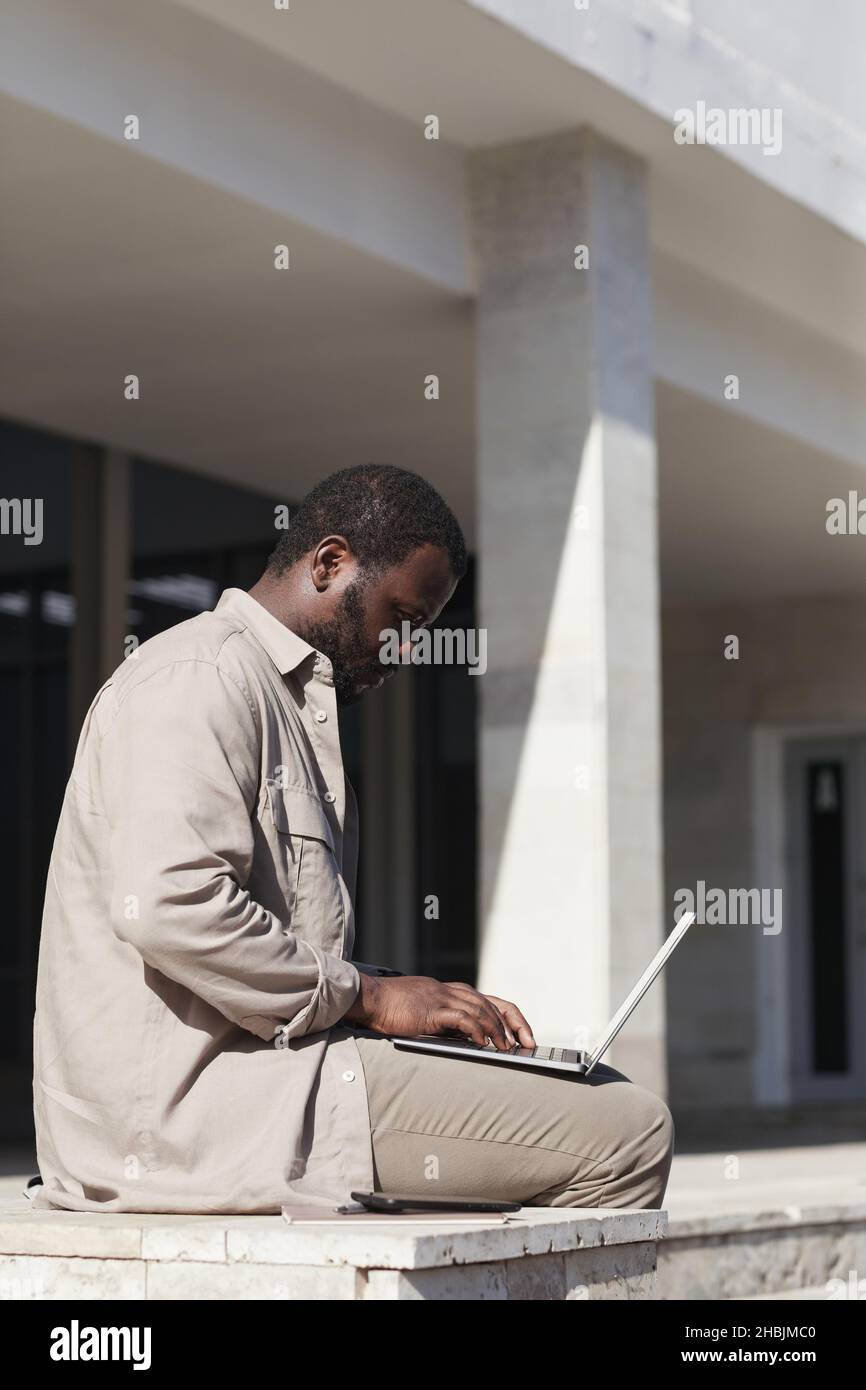 Side view portrait of black man using laptop outdoors in city lit by ...