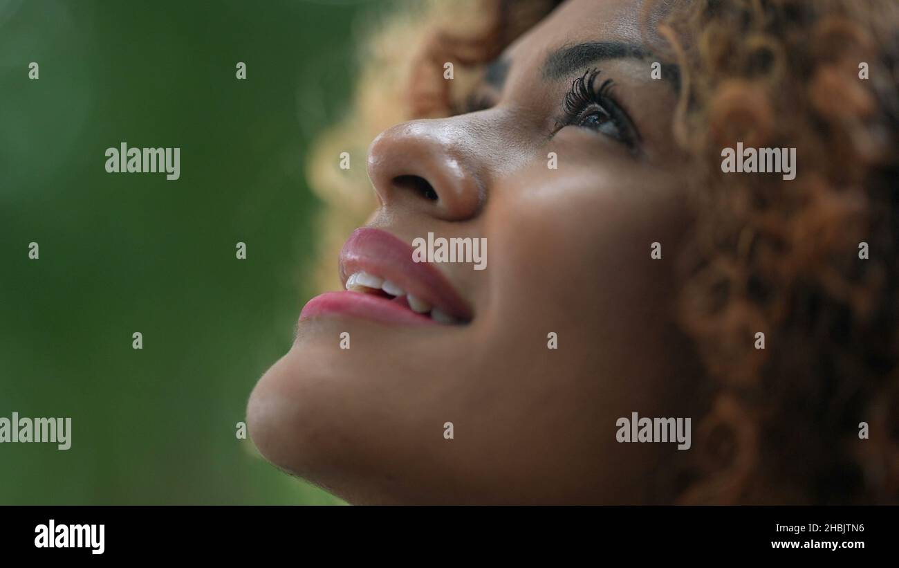 African woman taking a deep breath outside in nature looking up at sky ...