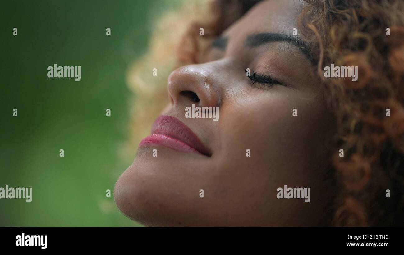 African woman taking a deep breath outside in nature looking up at sky ...
