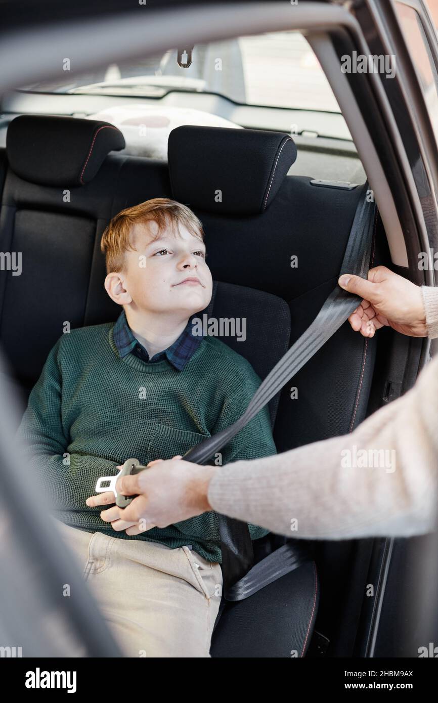 Vertical portrait of blonde boy buckling up in back seat of family car ...