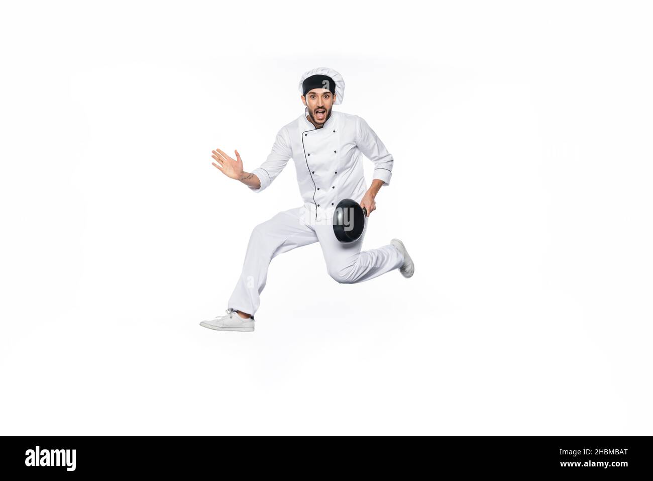 amazed chef in hat and uniform jumping and holding frying pan isolated ...