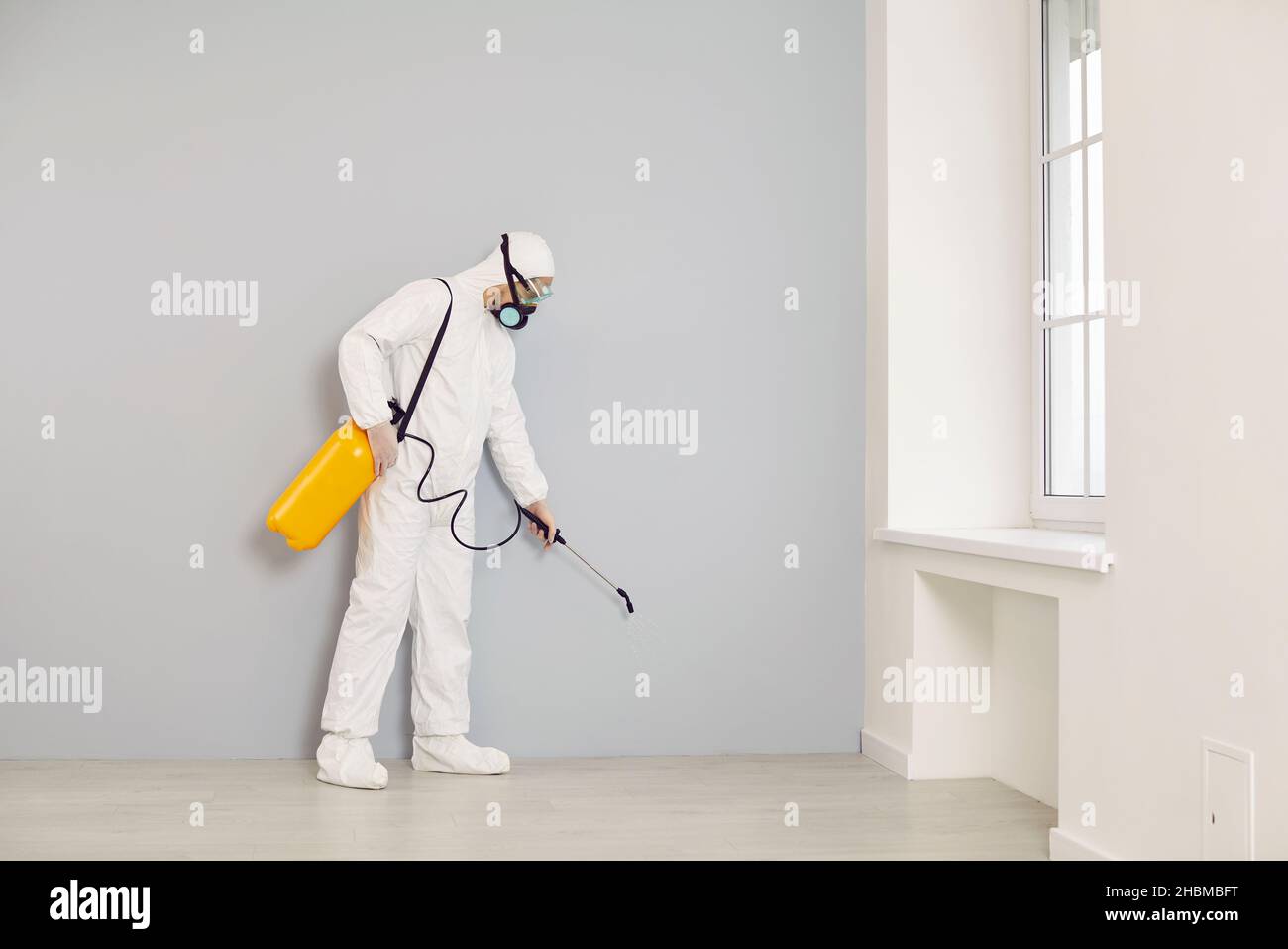 Pest control service worker in protective suit spraying insecticide in ...
