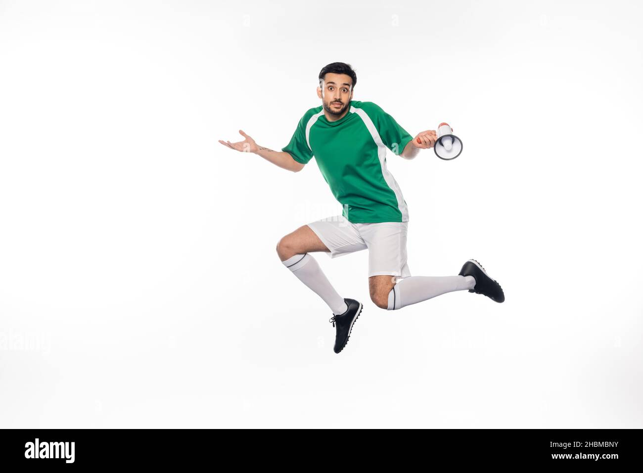 confused football player in uniform jumping and holding loudspeaker on ...
