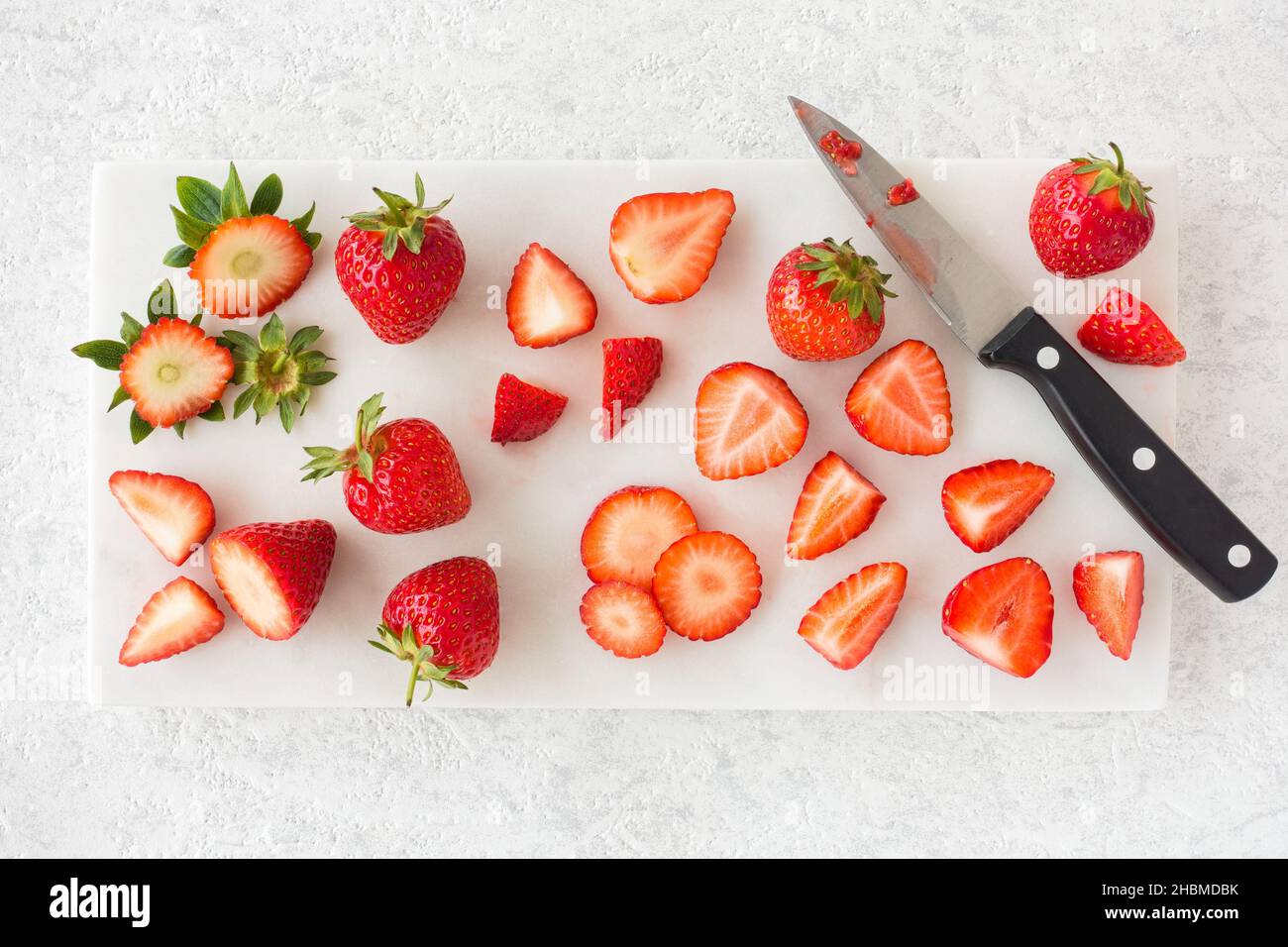 Closeup of cut and whole strawberries on white marble cutting board ...