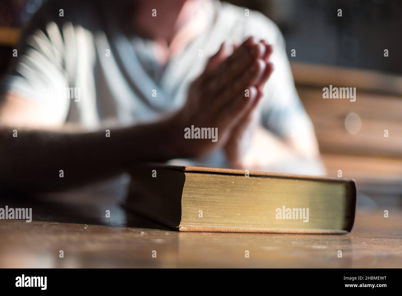 Man sitting at a table praying hands on a Bible Stock Photo - Alamy