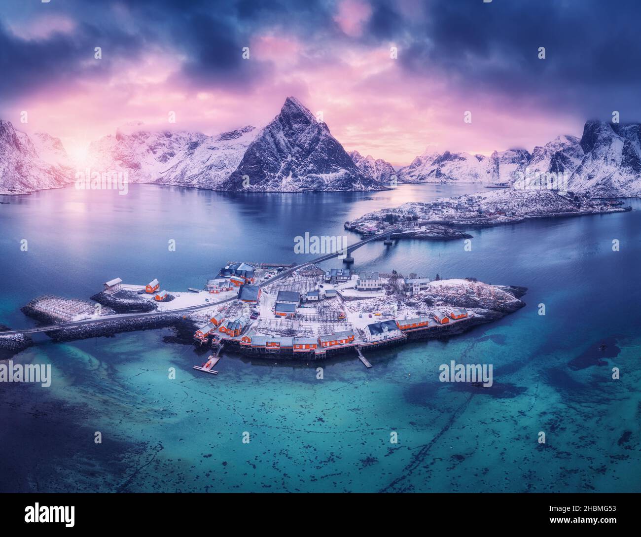 Aerial view of snowy islands with houses, rorbu, blue sea, mountains ...