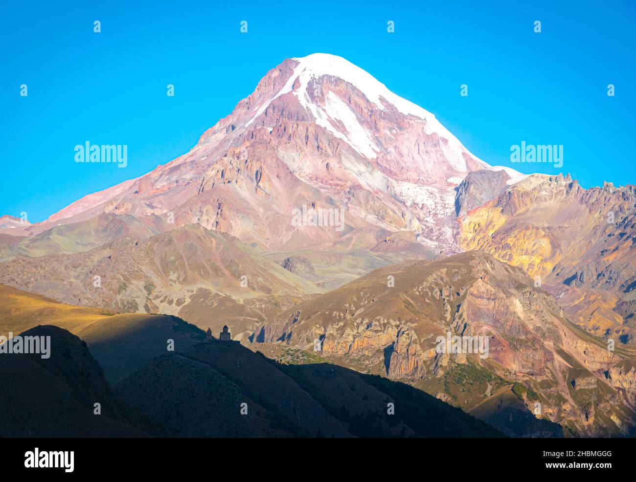 Red Kazbek mountain peak with yellow hills and Gergeti trinity ...