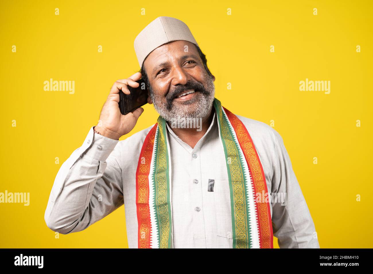 smiling Seniot Indian politician busy talking on mobile phone on yellow ...