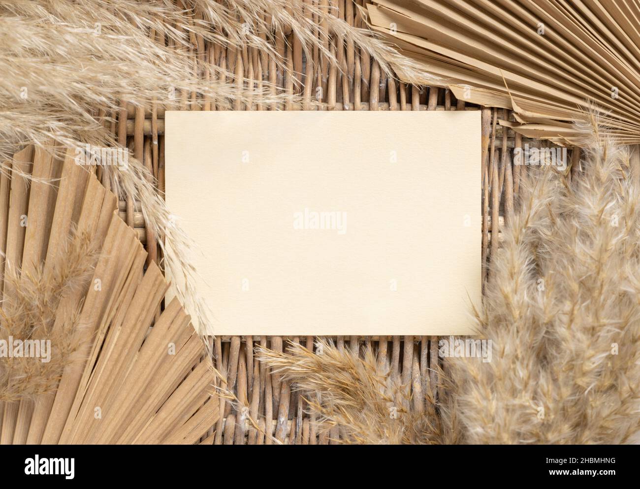 Boho scene with blank card on a wattled table near dry palm leaves and ...