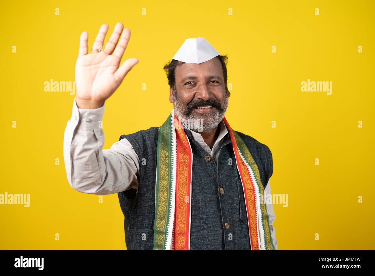 Senior Indan Politician greeting by waving hand on yellow studio ...