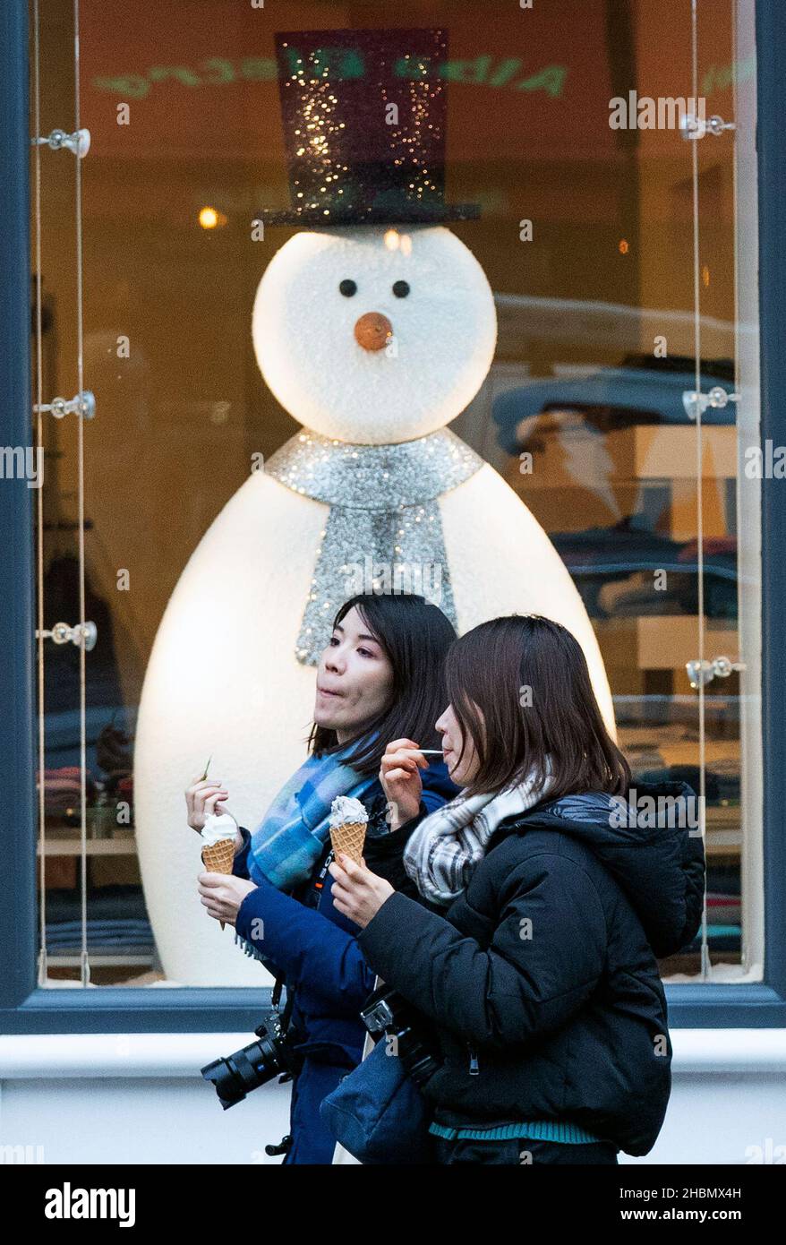 Members of the public eat ice cream as they walk past a snowman in a ...