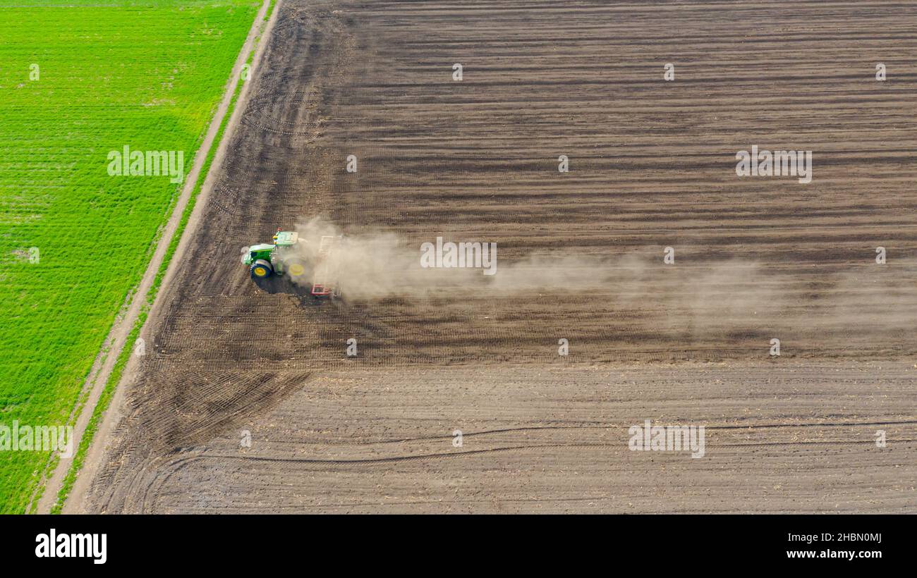 Above view of tractor as pulling machine, harrowing arable field ...
